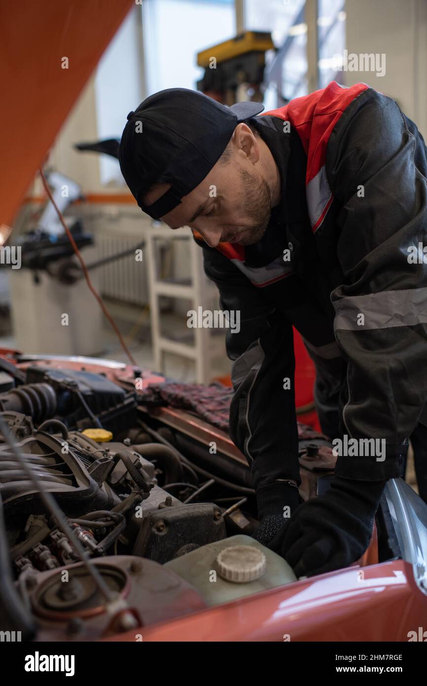 Vertical portrait of male mechanic looking under hood while repairing ...