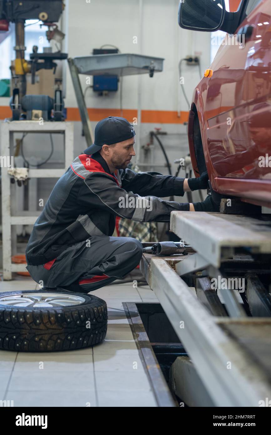 Side view full length portrait of male mechanic changing tires on car ...