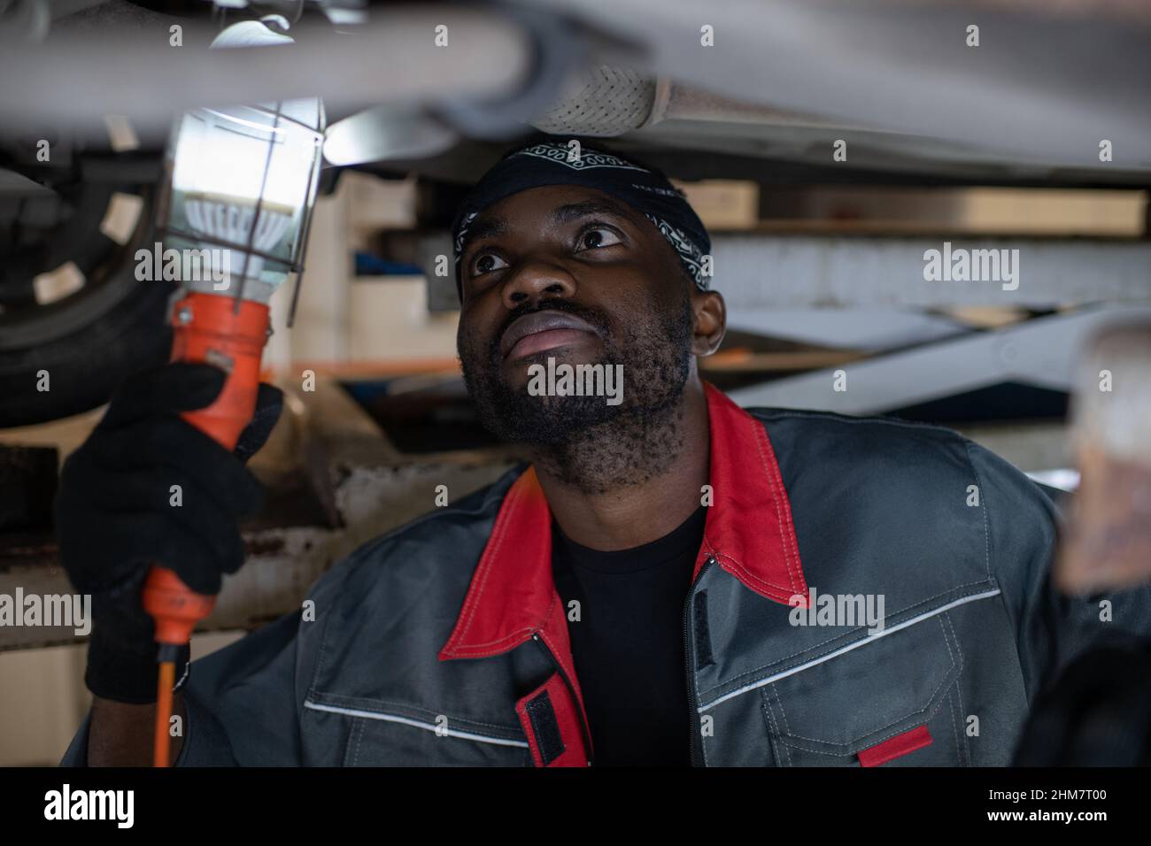 Portrait of African-American mechanic inspecting car on vehicle lift in ...