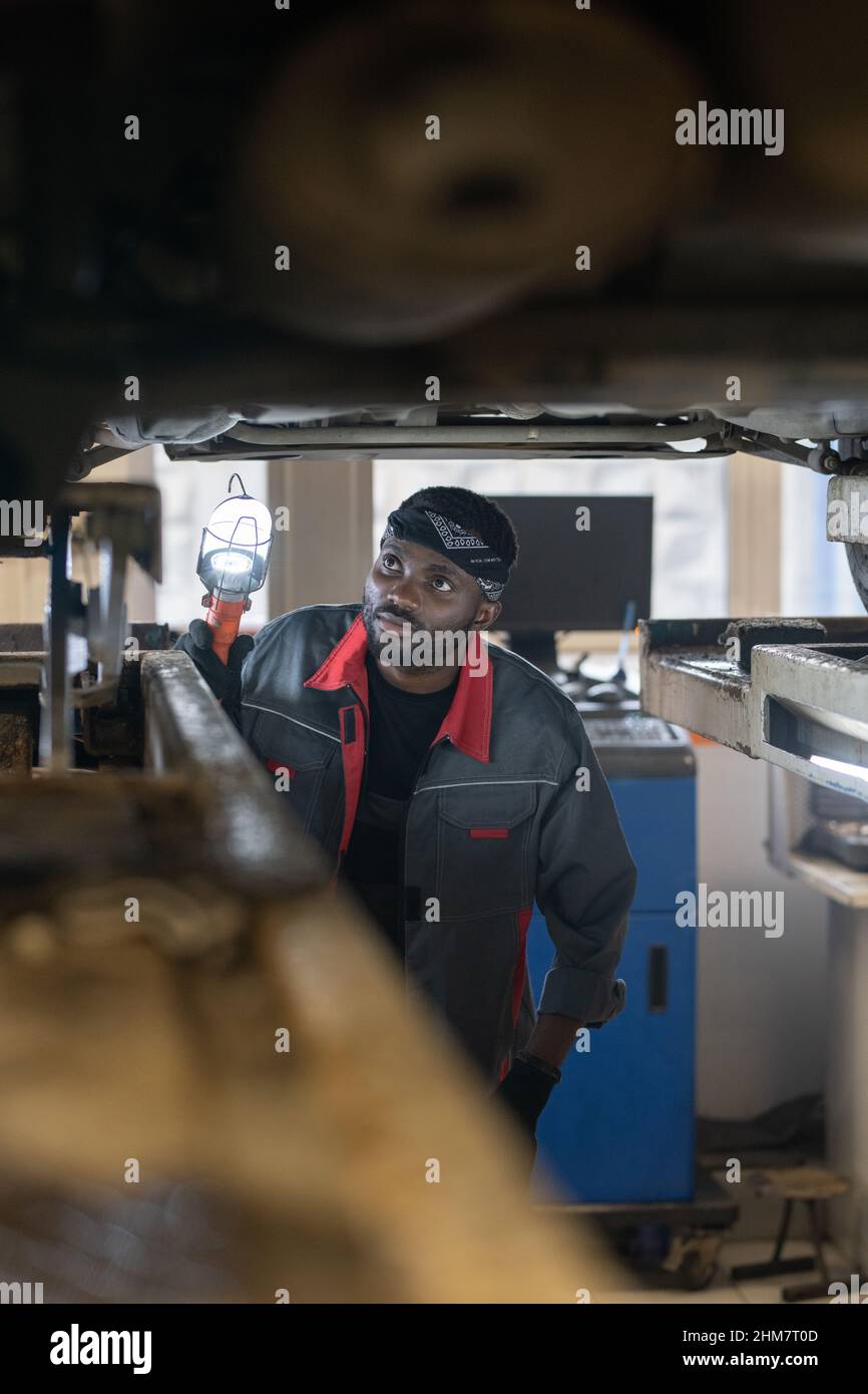 Vertical portrait of black car mechanic inspecting vehicle on lift in ...