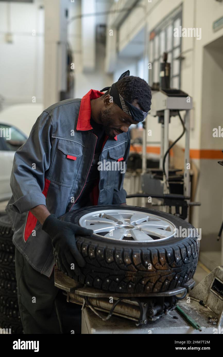 Vertical portrait of young black mechanic inspecting car tires while ...