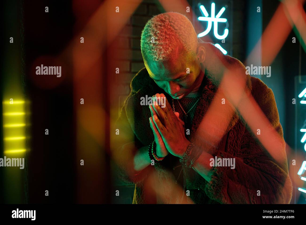 African cyberpunk man in fur coat praying in darkness with neon ...