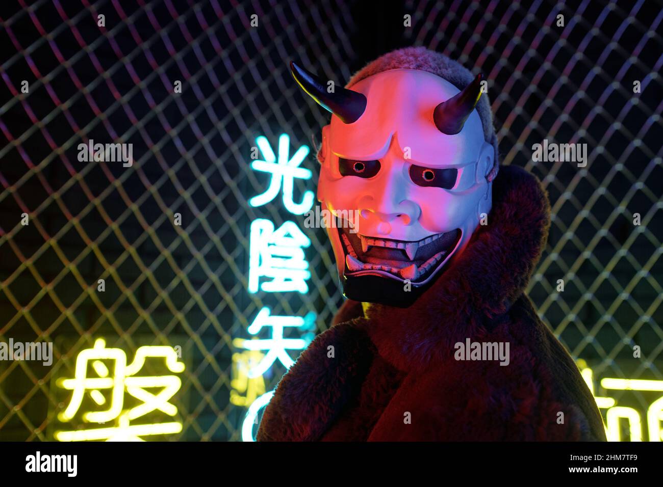 Close-up of cyberpunk guy in devil mask and fur coat looking at camera ...