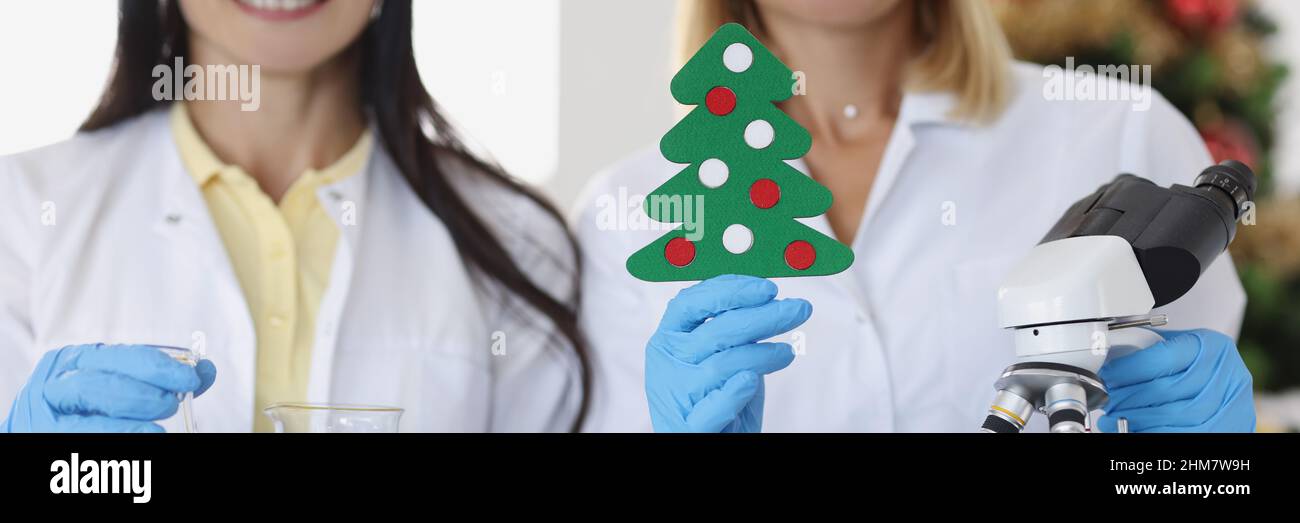 Two women in laboratory are holding microscope and test tubes closeup ...