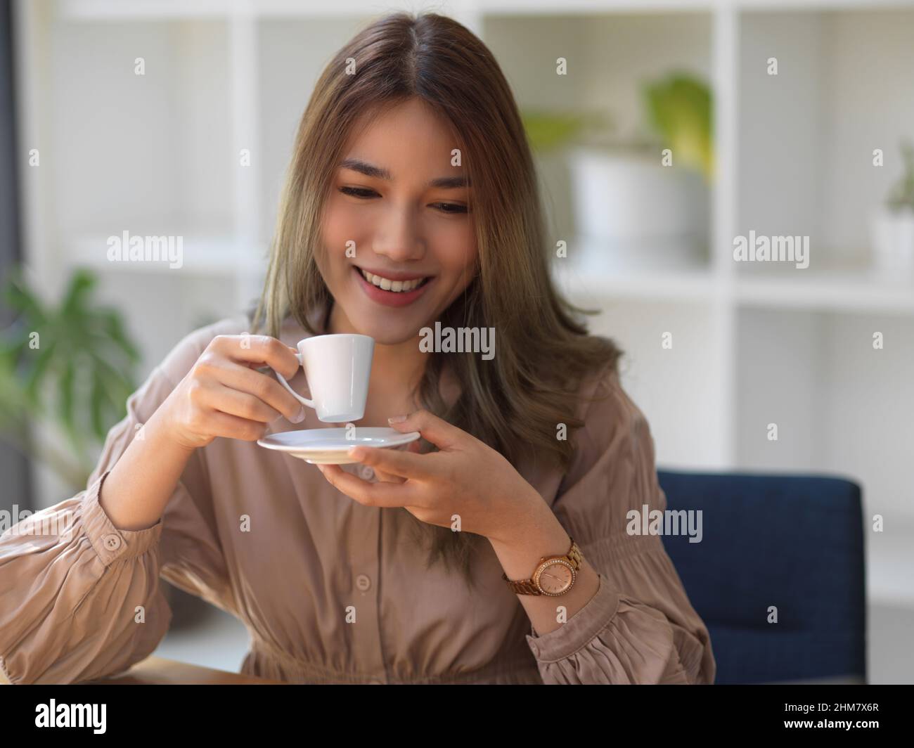 A charming Asian woman holds a coffee set and sips hot morning coffee ...