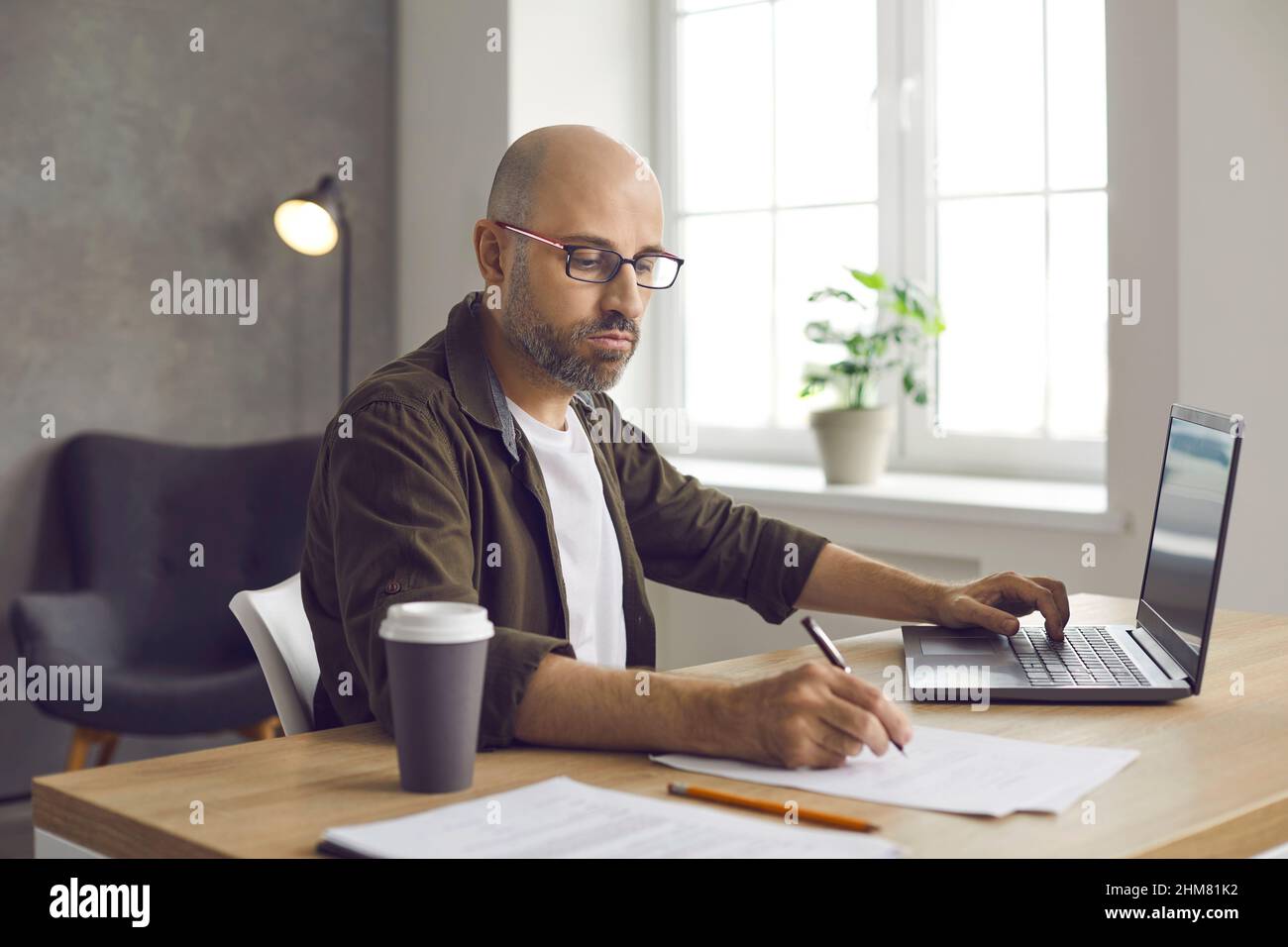 Serious man sitting at desk in home office, working on laptop computer ...