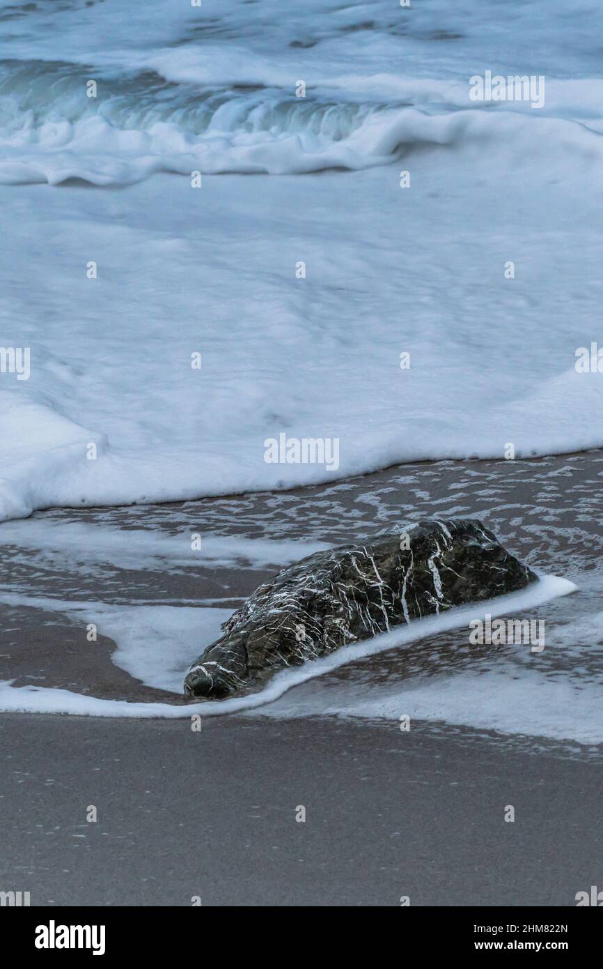 Incoming tide flowing around a rock on a beach Stock Photo - Alamy