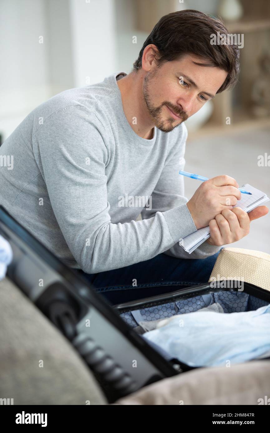 man writing list while packing his suitcase Stock Photo - Alamy