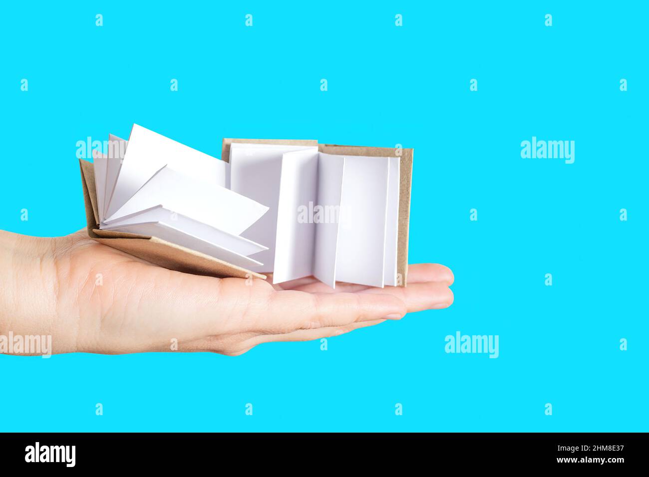 Two miniature handmade books with blank pages in hand isolated on blue ...