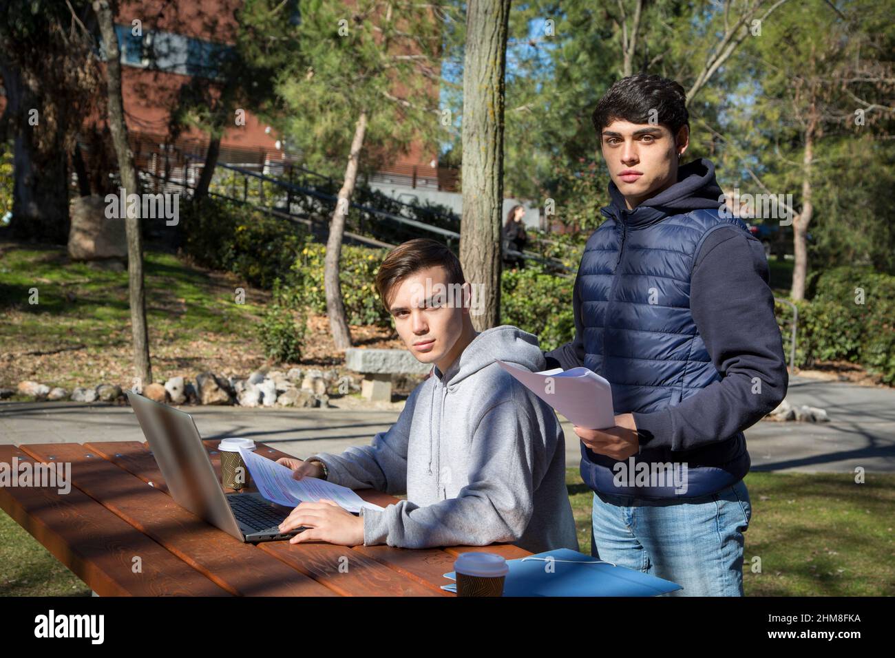 two university students looking at a laptop computer on a table outside ...