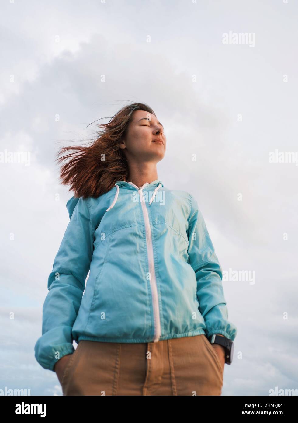Portrait of a young woman in a blue windbreaker in windy weather. A ...