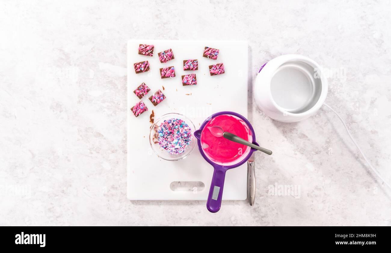 Flat lay. Drizzling melted pink chocolate on top of the mini chocolates ...