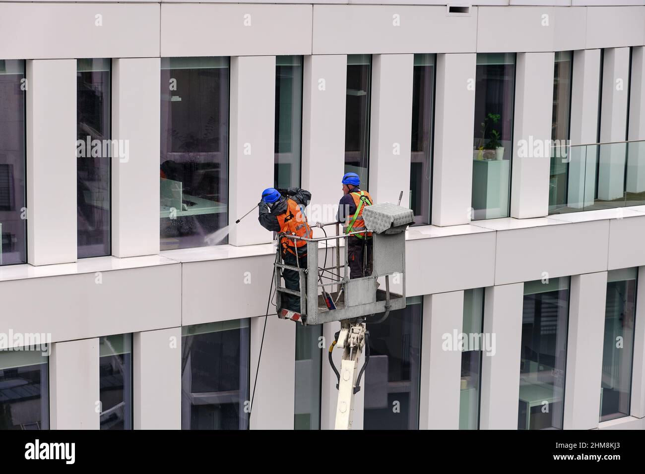 Two workers wearing safety harness wash office building facade at ...
