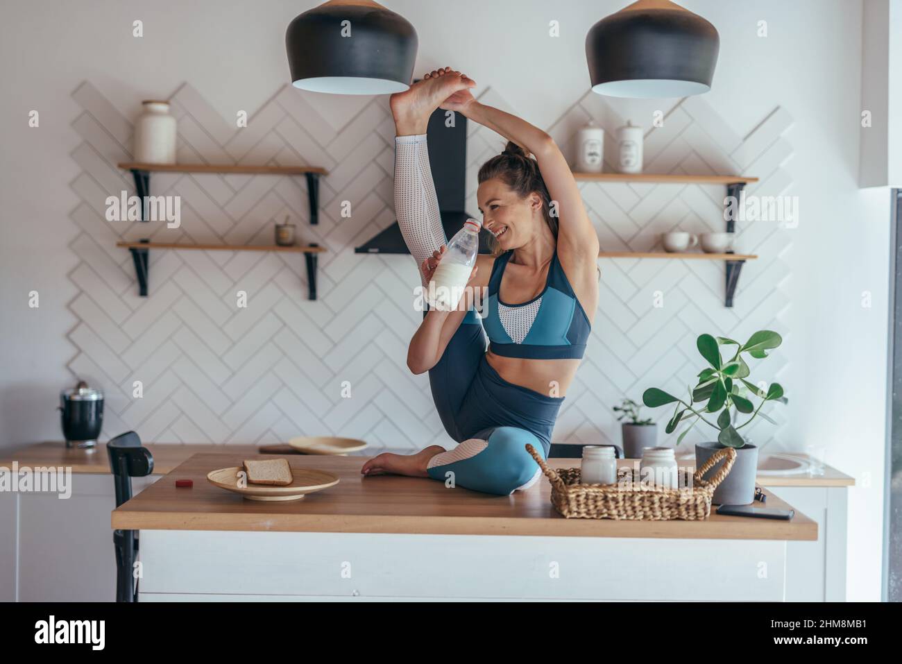 Girl stretches and eats breakfast at the same time on kitchen table ...