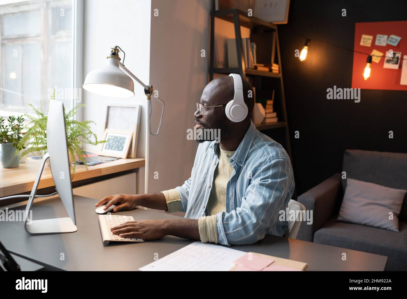 African man in wireless headphones sitting at his workplace in front of ...
