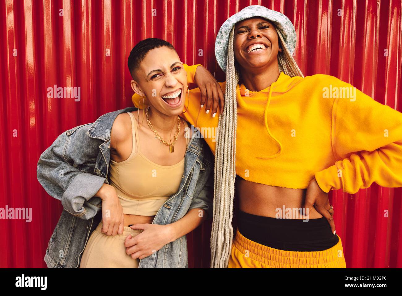 Two best friends laughing happily while standing together against a red ...