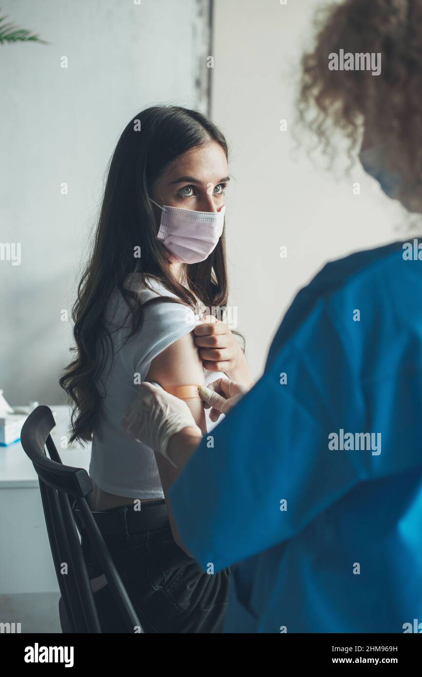 Back view of a nurse applying a adhesive patch to a woman arm after ...