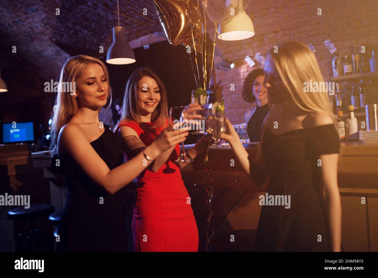 Happy young women with glasses of wine and cocktails enjoying a night ...