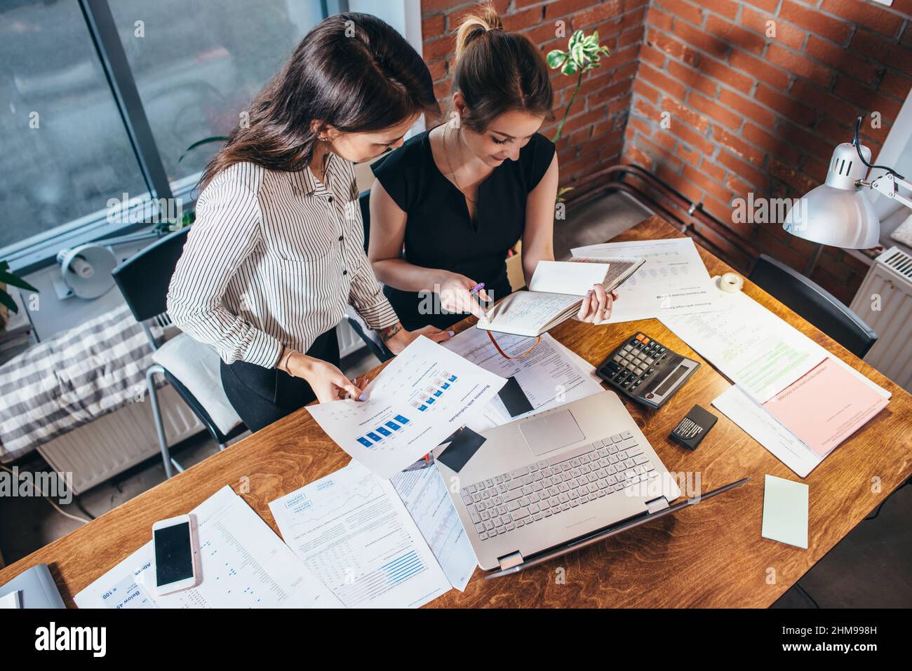 Top view of two female colleagues and desk covered with papers and ...