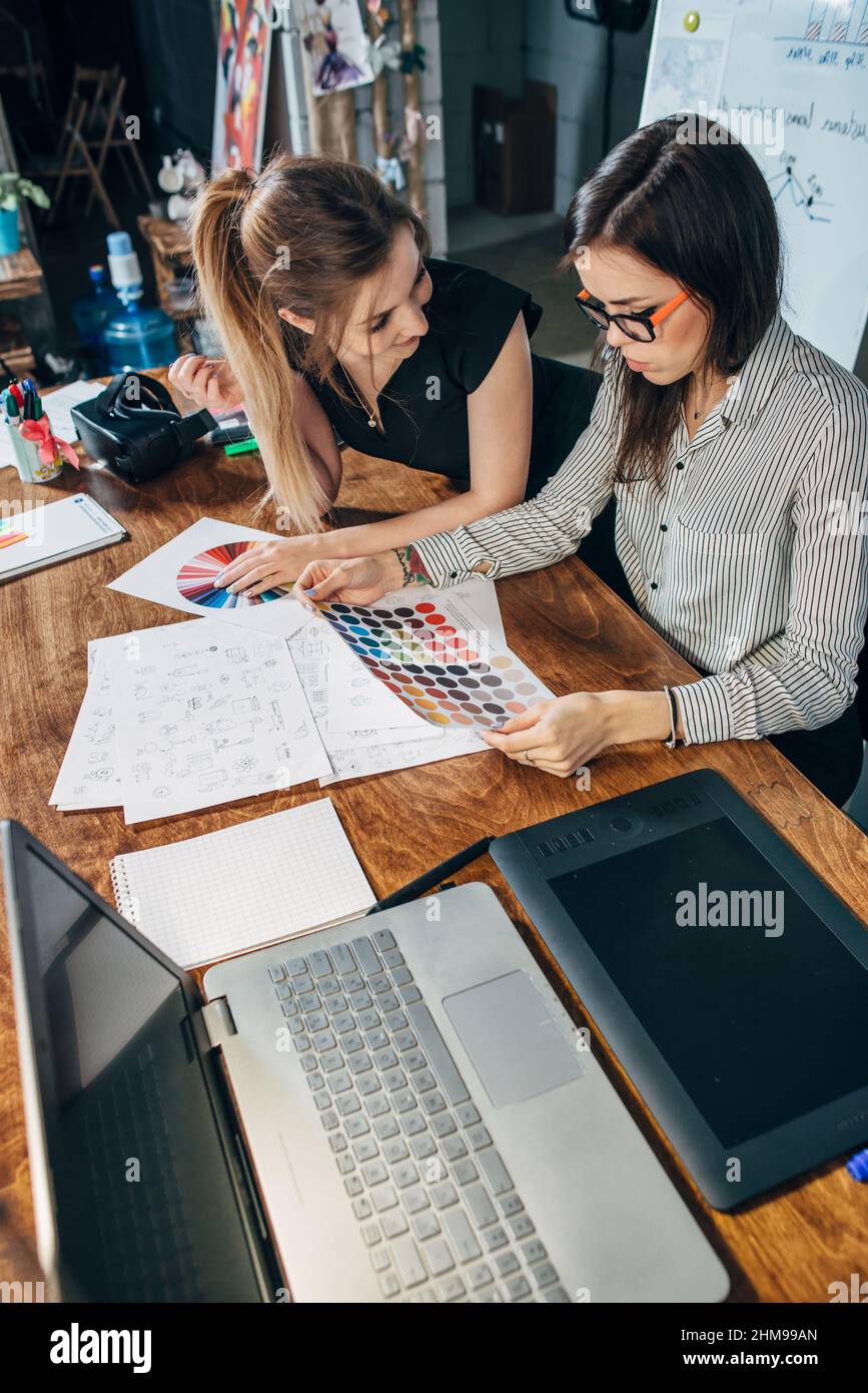 Young female graphic designers sitting at desk with laptop, color ...