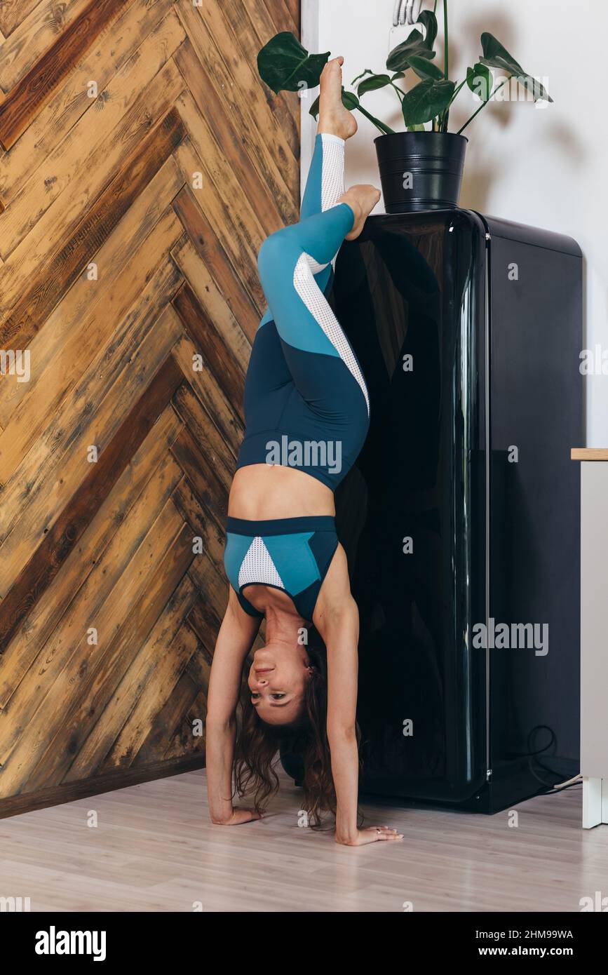 Fit woman in the kitchen doing handstand leaning on the refrigerator ...
