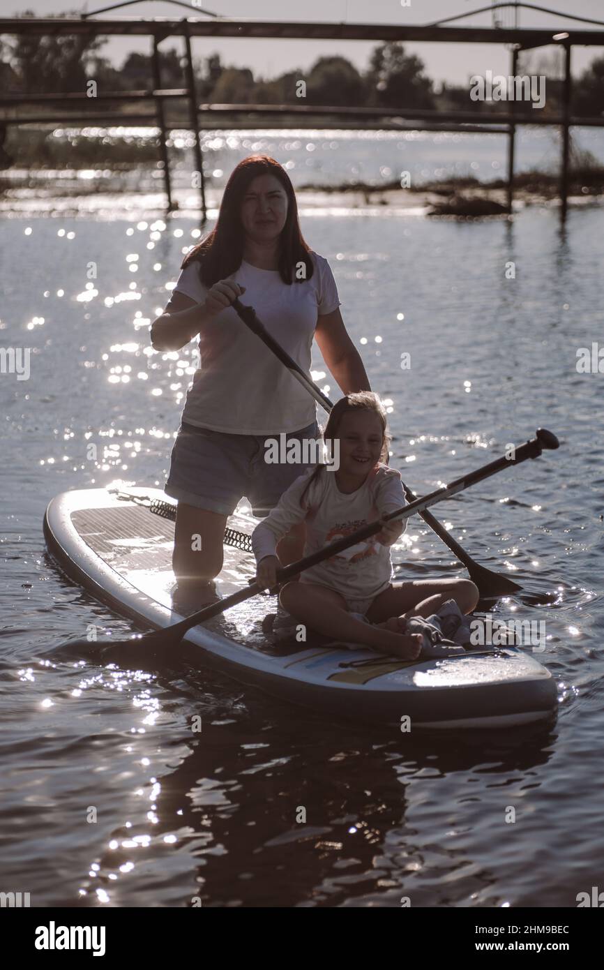 Female child with mother sup boarding with oars in hands smiling and ...