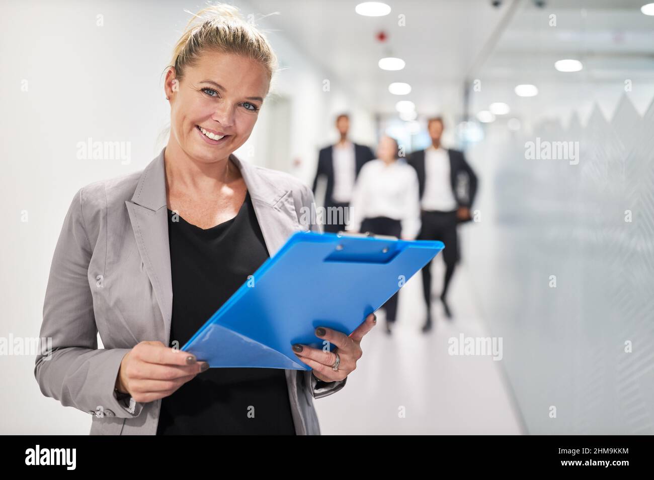 Smiling business woman with checklist on clipboard in hallway of office ...