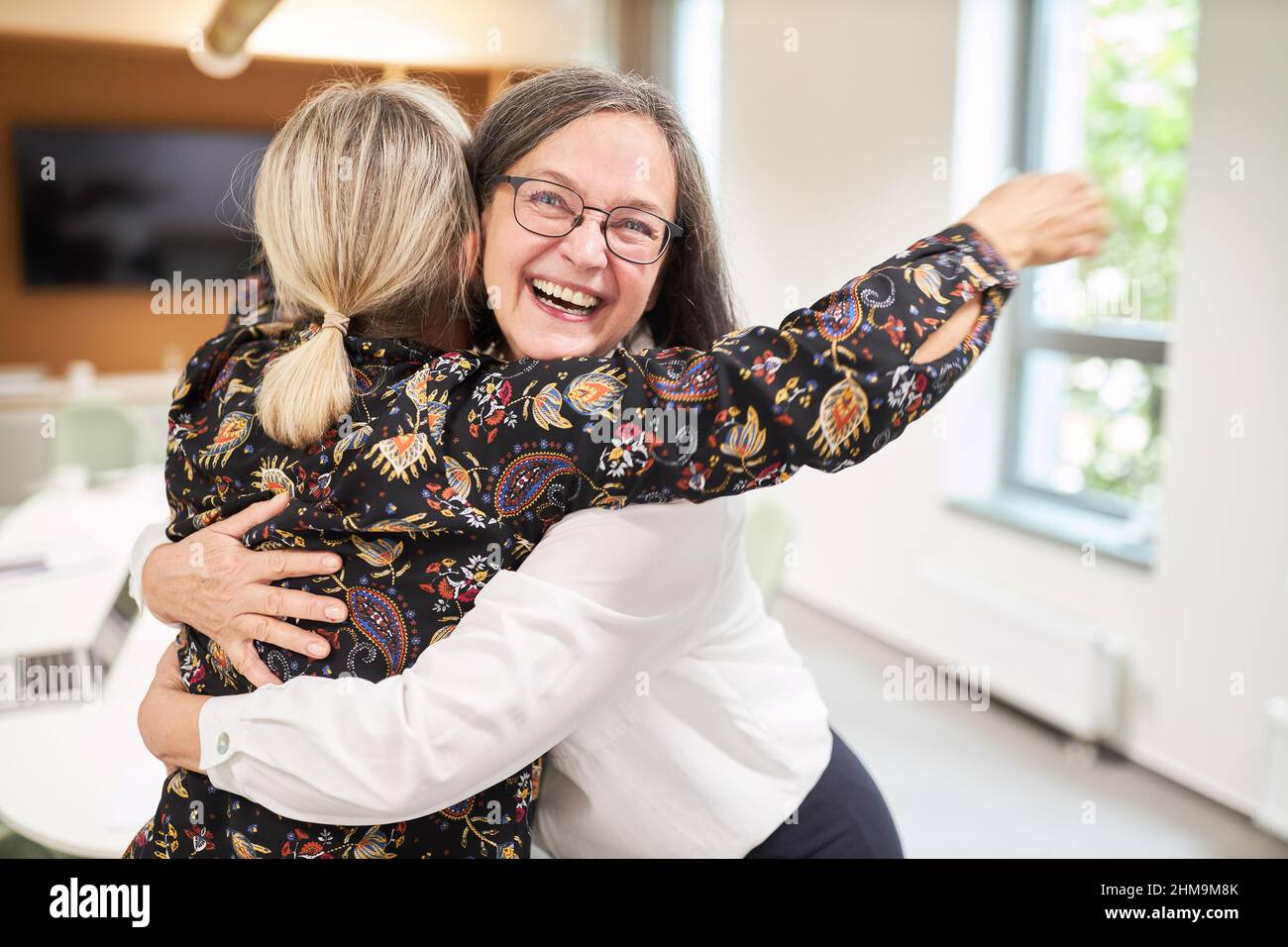 Two happy business women hugging to say hello or celebrating a ...