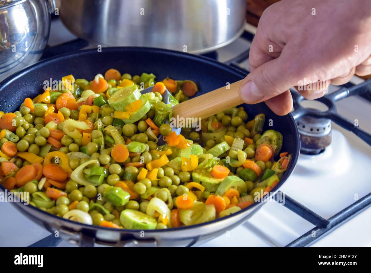 Process of cooking saute at home. Man's hand mixes stewed vegetables in ...