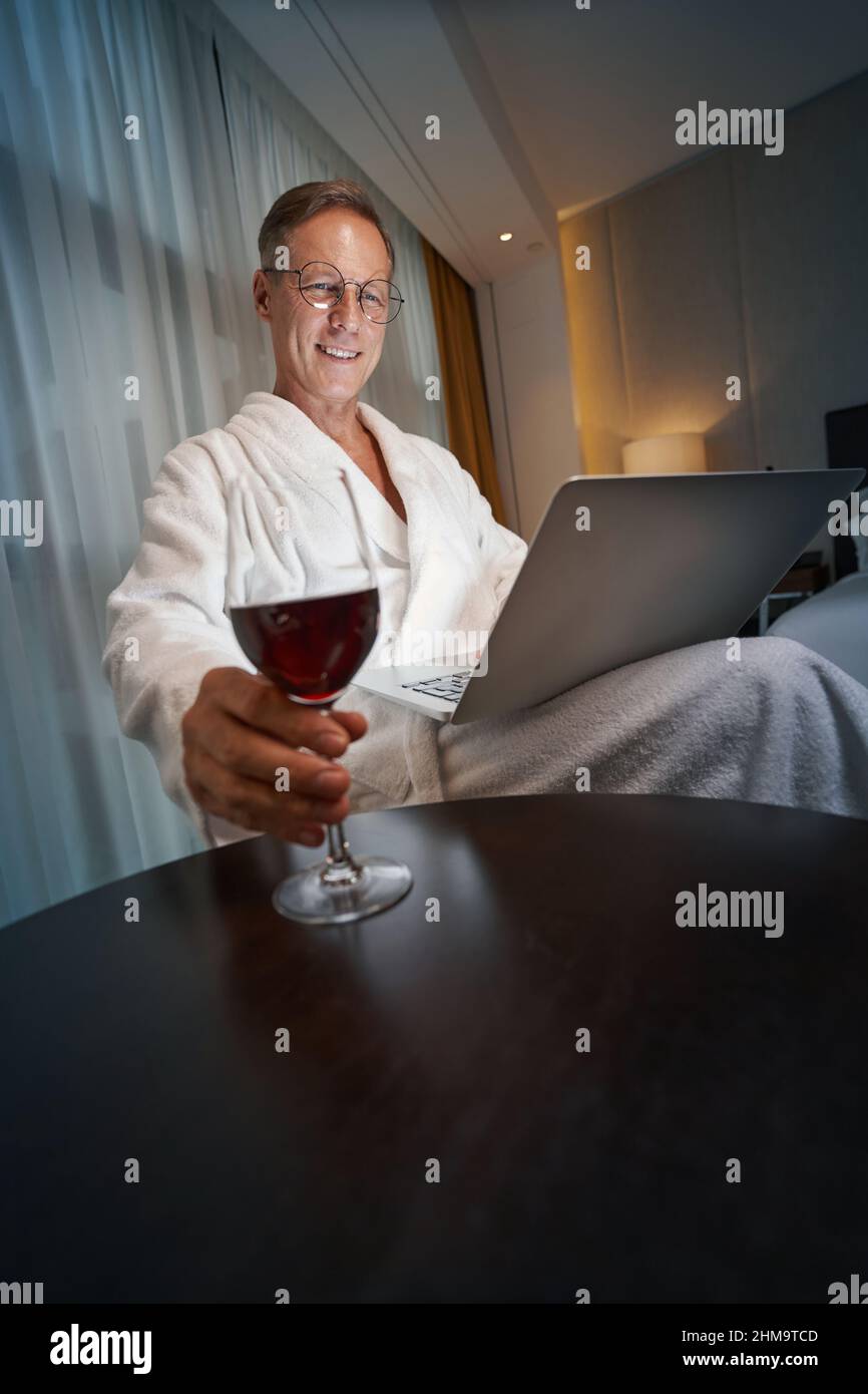 Amicable man relaxing with wine and getting some work done Stock Photo ...