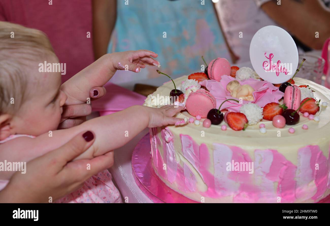Girl newborn 1-year-old with hands touching cake during birthday party ...