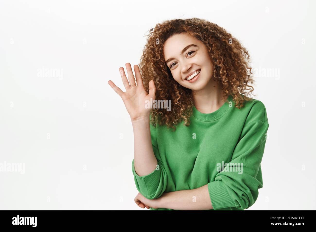 Portrait of beautiful girl saying hello, waving hand at camera friendly ...