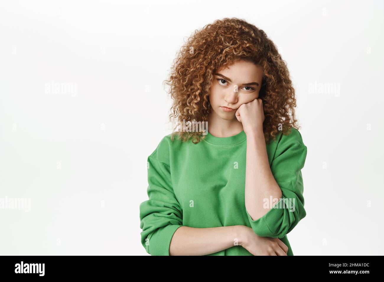Moody and bored curly girl sulking, lean head on fist and staring with ...