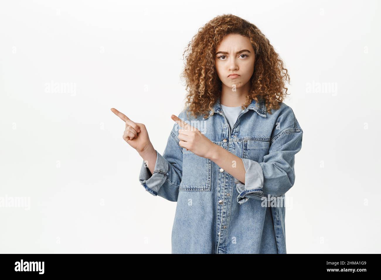 Angry curly young woman, pointing fingers left, frowning upset and ...