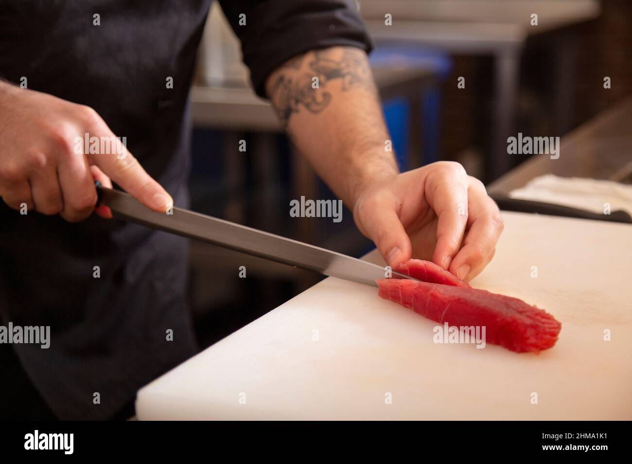 Cropped unrecognizable male cook in uniform cutting raw fish with knife ...