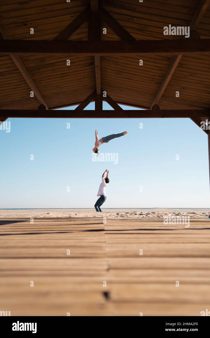 Side view of distant unrecognizable man throwing female acrobat up in ...