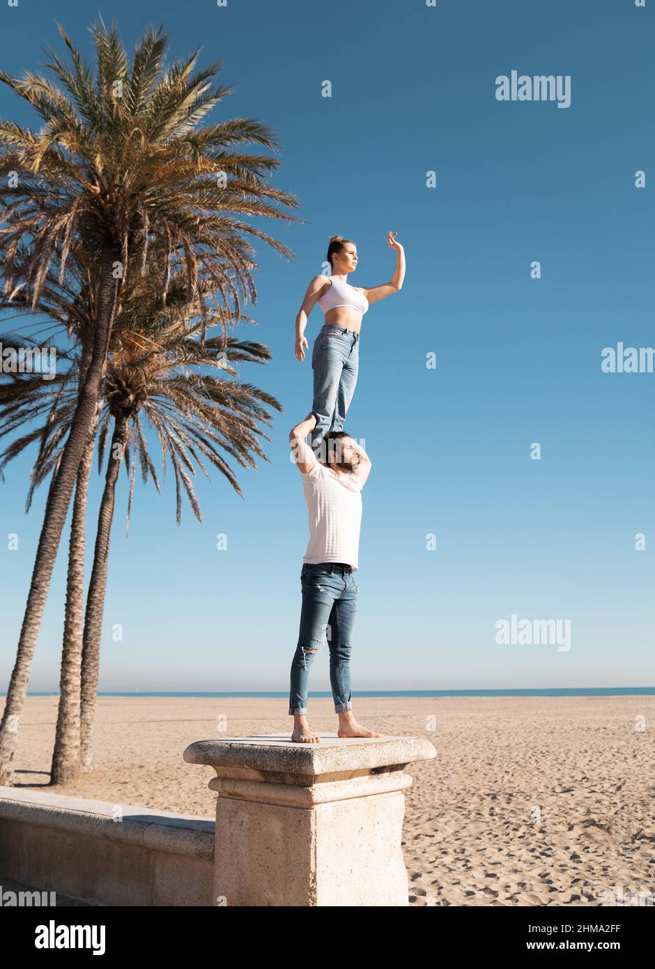 Full body of active female acrobat standing on shoulders of man while ...