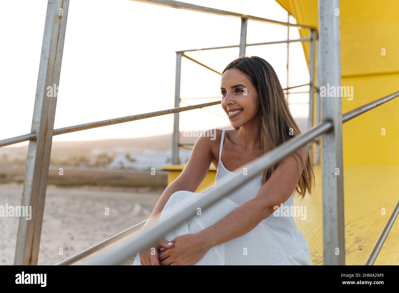 Young female traveler in white dress with straw hat leaning on railing ...