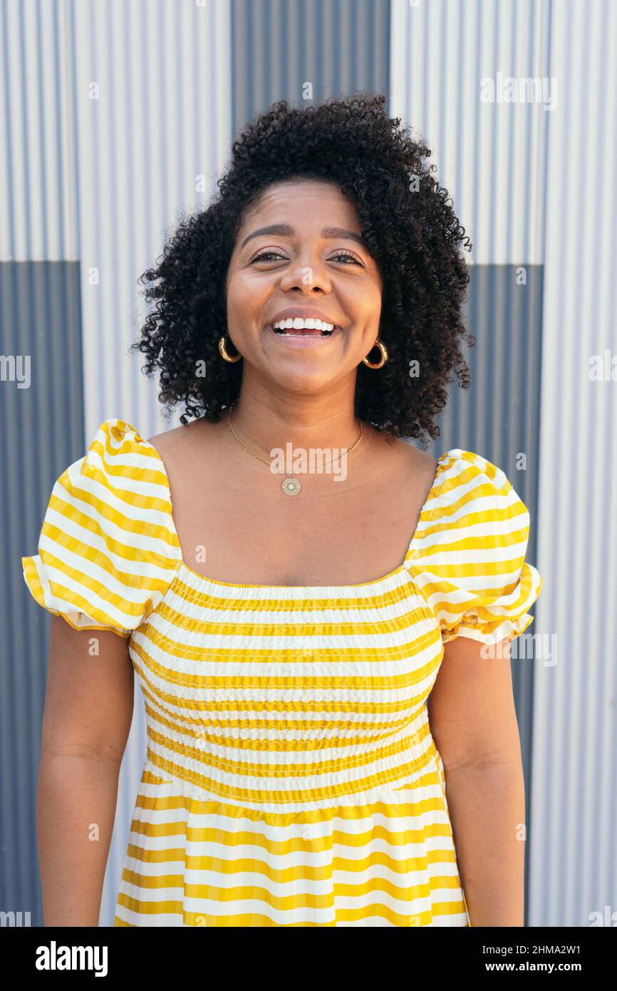 Happy Hispanic female with curly hair standing near metal background ...