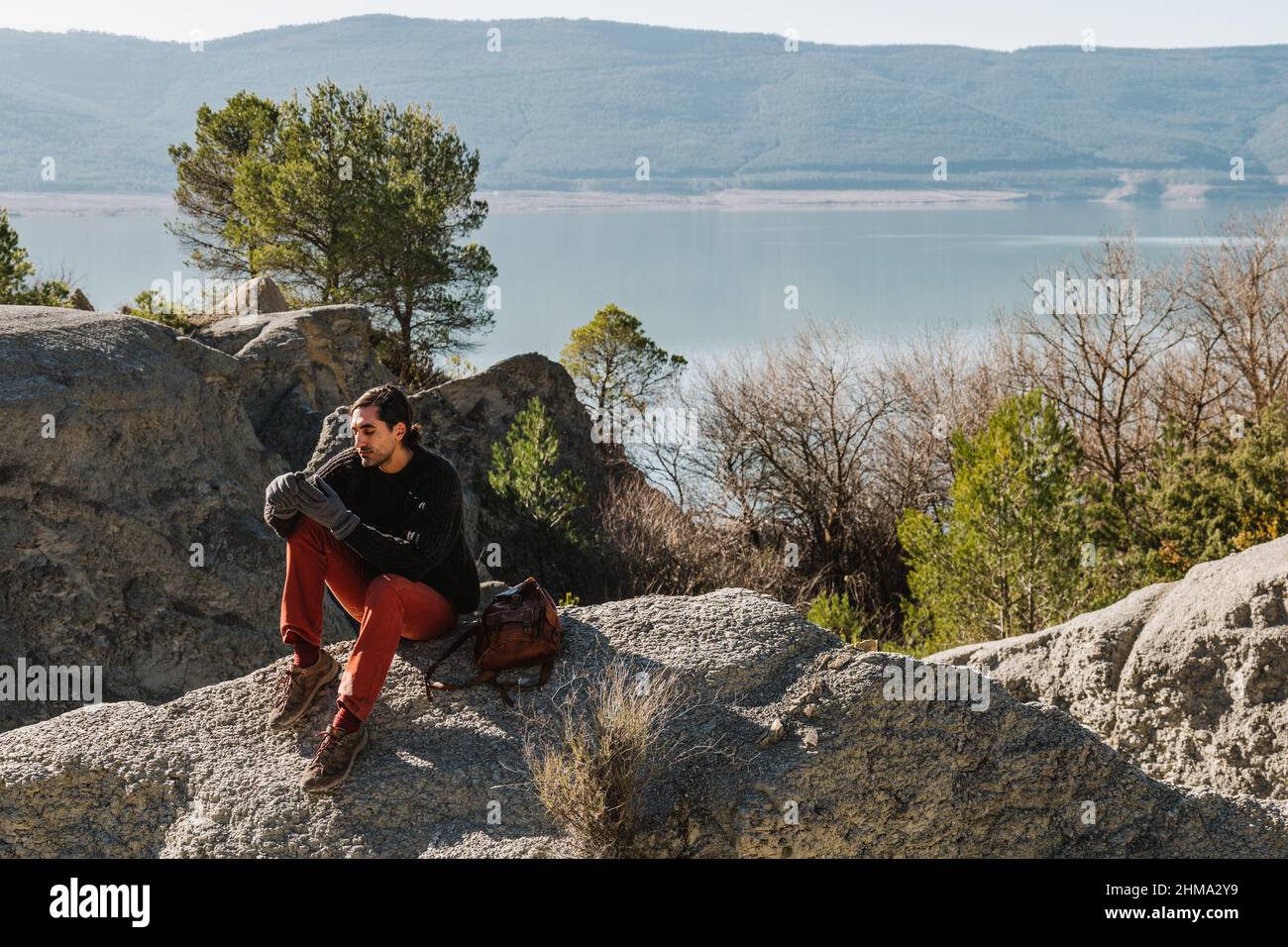 Full body of relaxed male enjoying sunshine on rocky formation on shore ...
