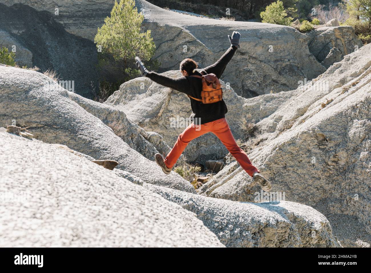 Back view full body of male explorer raising arms while jumping from ...