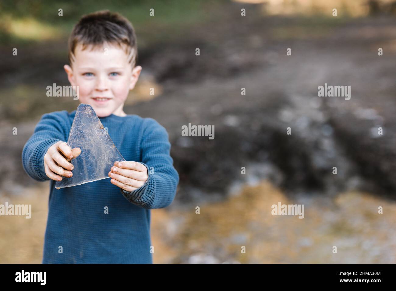 Cute boy standing with transparent piece of cold ice in autumn woods ...