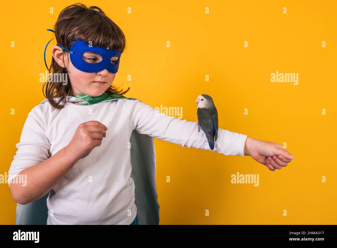 girl dressed as superhero holding parrot on arm against yellow backdrop ...