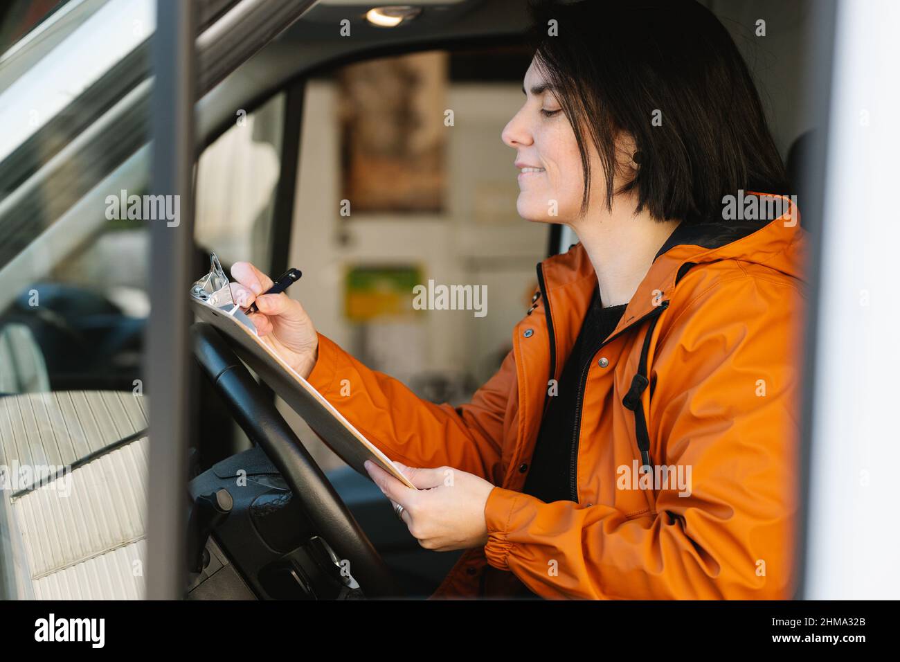 Side view of female driver writing notes on clipboard while sitting in ...