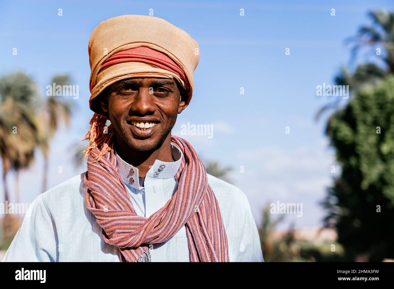 Cheerful Arab male wearing traditional turban looking at camera and ...