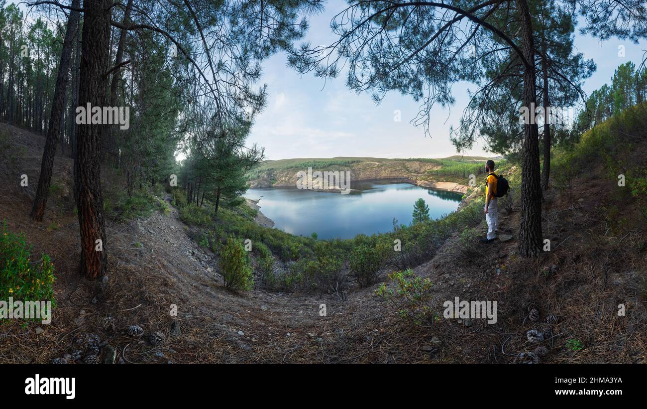 Wide angle side view of distant anonymous male hiker standing near lake ...