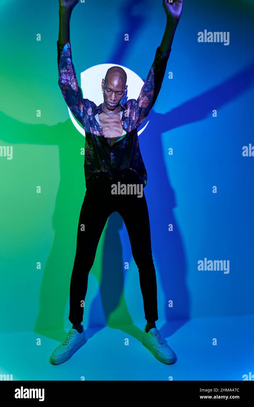 Full body of bald African American male in stylish wear raising arms ...