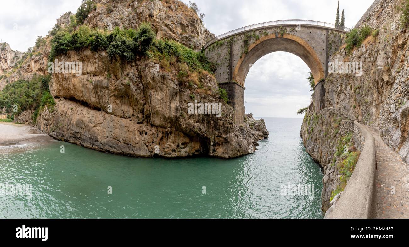 Wide angle of old arched bridge over rippling sea located amidst rough ...