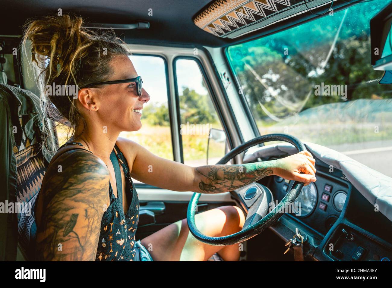 Side view of female traveler in sunglasses sitting at steering wheel ...