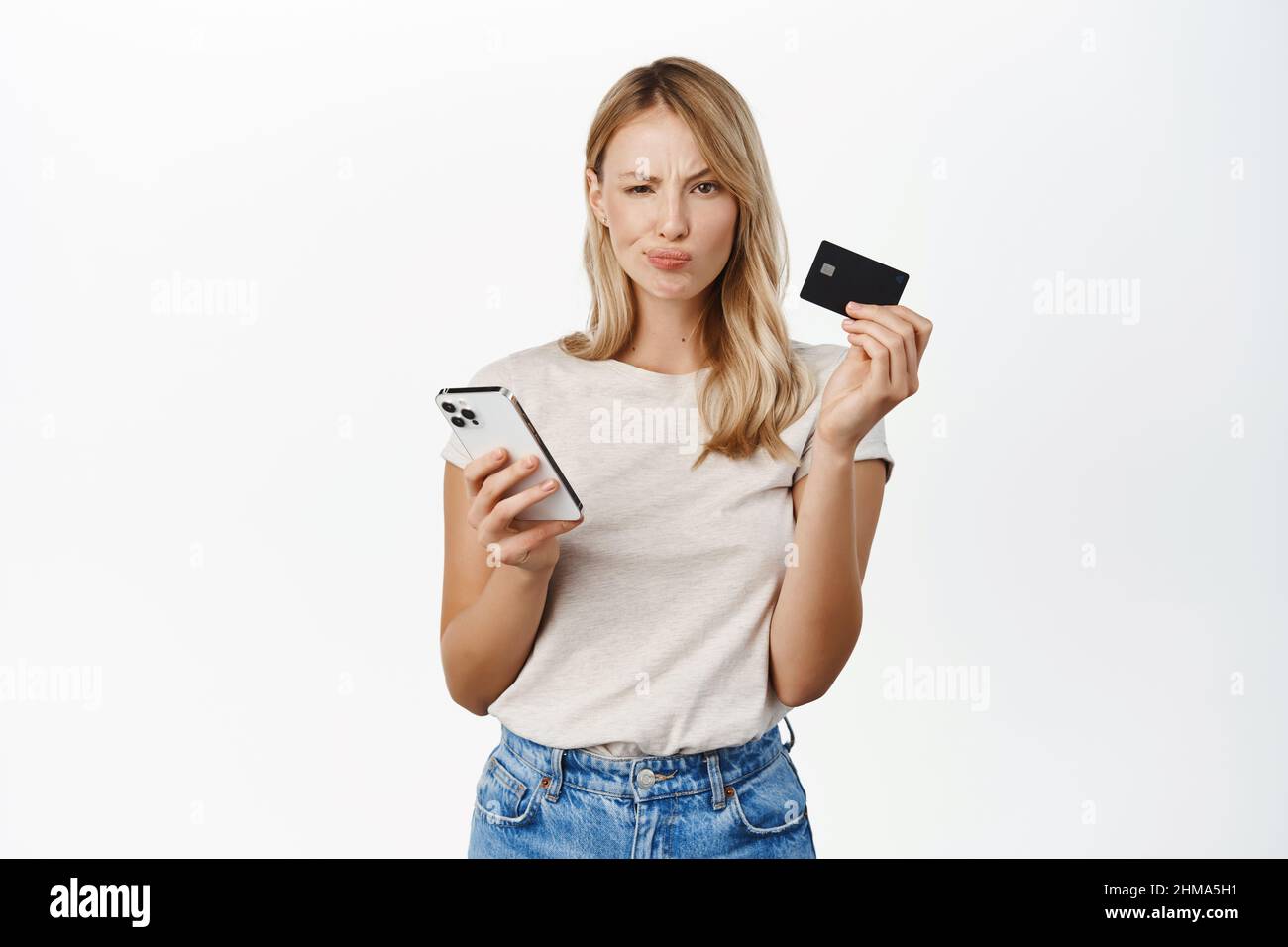 Skeptical young woman shopper frowning, showing credit card, holding ...